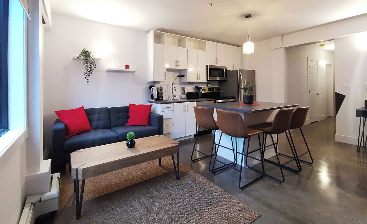 Cozinha moderna com armários brancos, micro-ondas e geladeira. Há uma área de jantar com mesa e cadeiras de madeira.