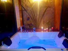 Uma banheira de hidromassagem com um banco de madeira, velas e uma planta ao fundo.