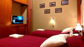 Quarto de hotel com duas camas, uma televisão à esquerda e uma parede com quatro quadros emoldurados.