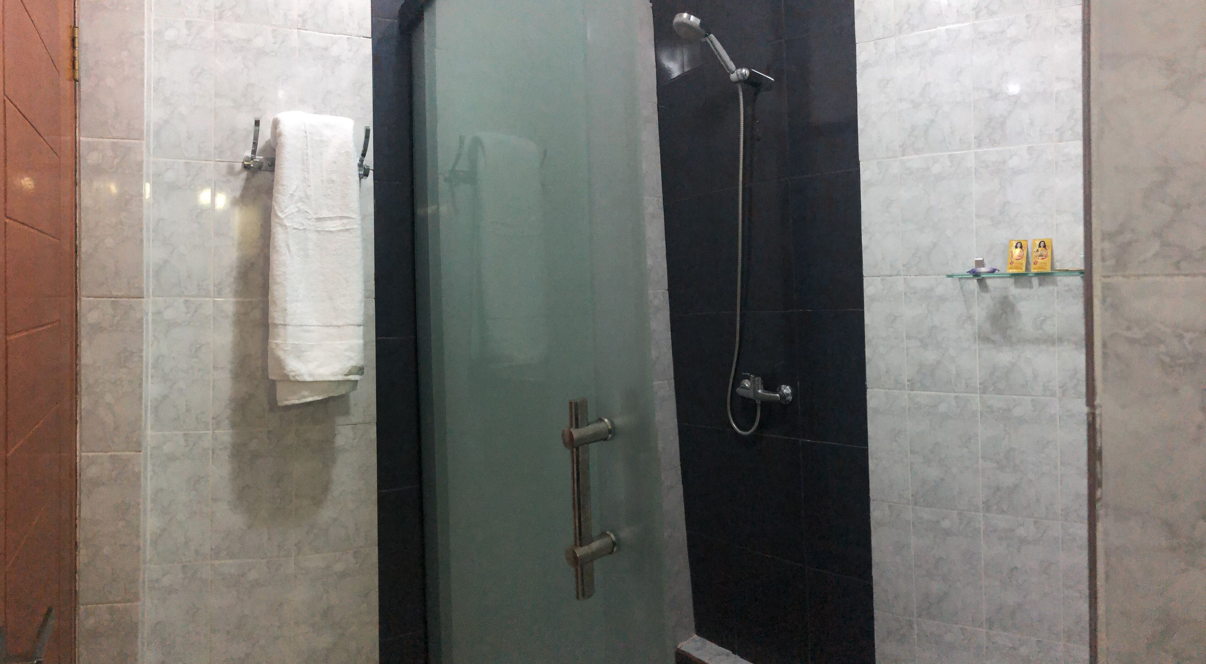 Um banheiro com chuveiro em box de vidro, porta-toalhas e prateleira com artigos de higiene pessoal.