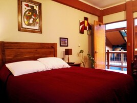 Quarto com uma cama grande, cabeceira de madeira, um quadro na parede e uma porta que dá para outro cômodo.