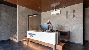 Balcão de recepção com a inscrição "THE BAGAN SUITE", design moderno, um computador e uma pessoa sentada atrás dele.
