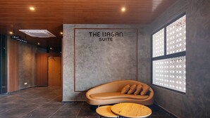 Um lobby moderno com um sofá e duas mesas redondas, uma placa com a inscrição "The Ibagan Suite" e uma janela grande com um padrão de treliça.