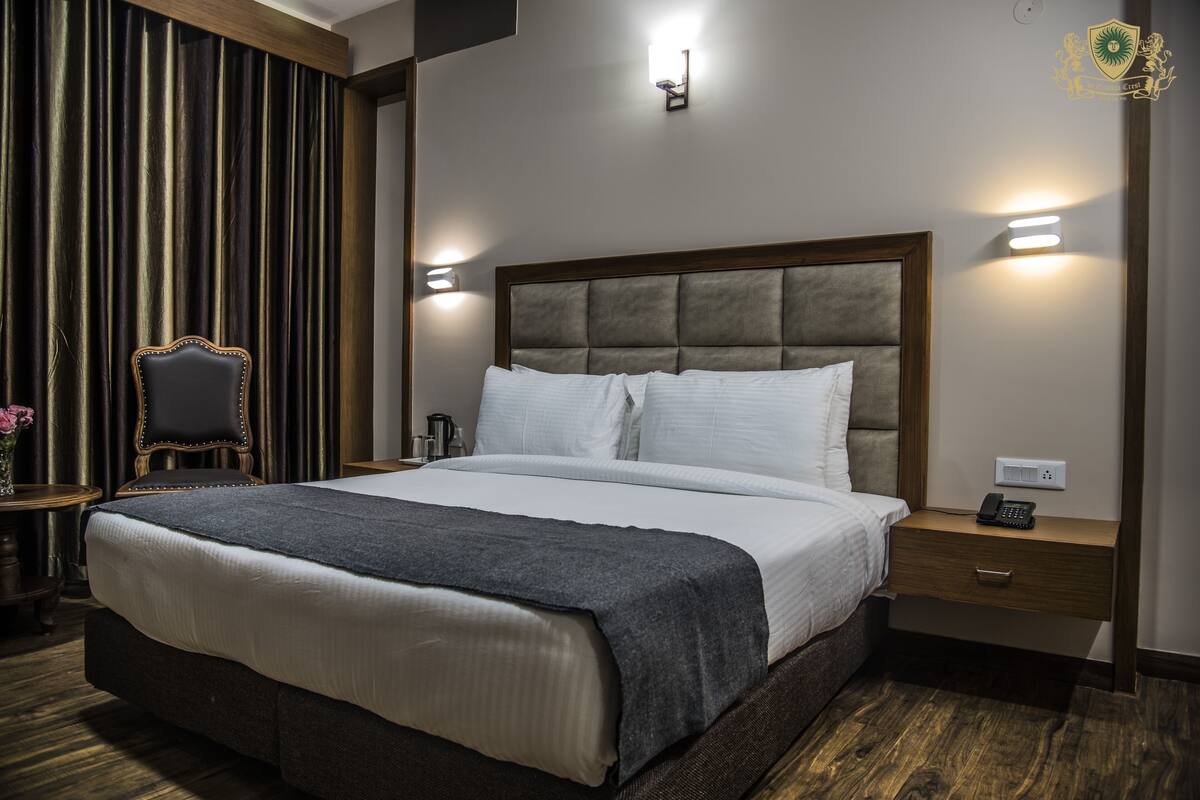 Cama bem arrumada com cabeceira cinza, mesa de cabeceira com telefone e luminária fixada na parede.