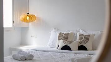 Quarto com cama, roupa de cama branca, luminária pendente e aparelho de ar condicionado.