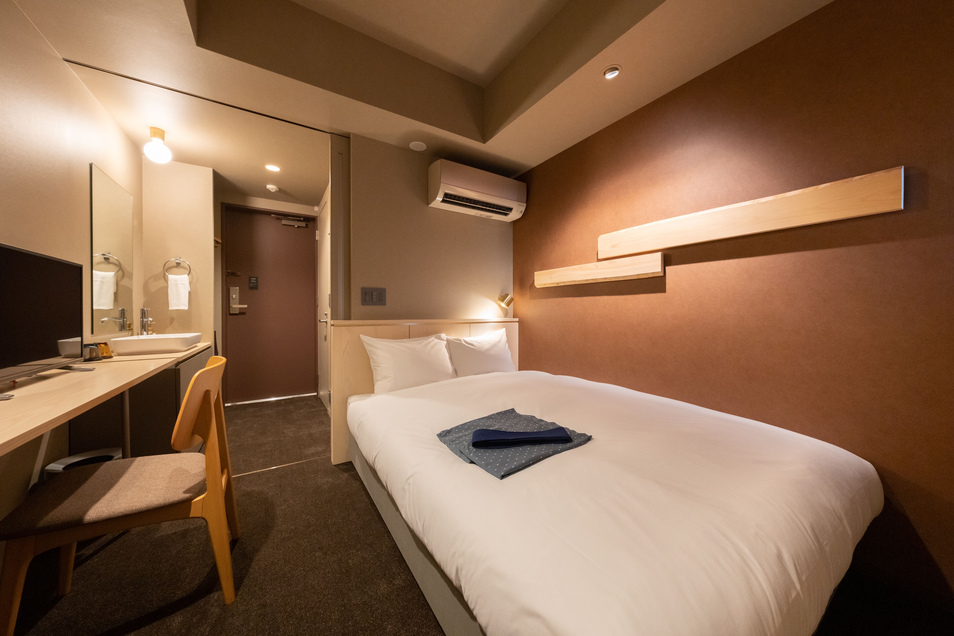 Quarto de hotel com cama, escrivaninha, cadeira, espelho e ar condicionado.