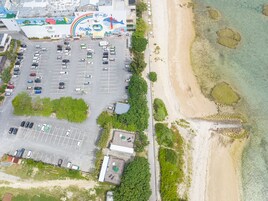 Vista aérea de um estacionamento ao lado de uma praia com águas cristalinas e alguma vegetação.