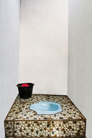 Casa de banho pequena com azulejos, lavatório azul e um balde preto.