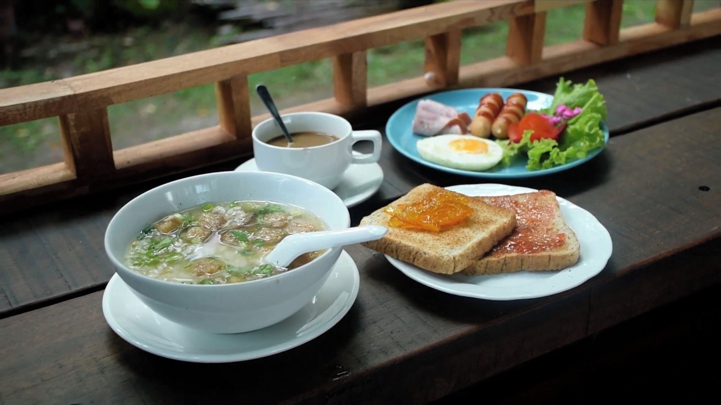Uma refeição com sopa, torradas com geleia, ovo cozido e uma salada sobre uma mesa de madeira.