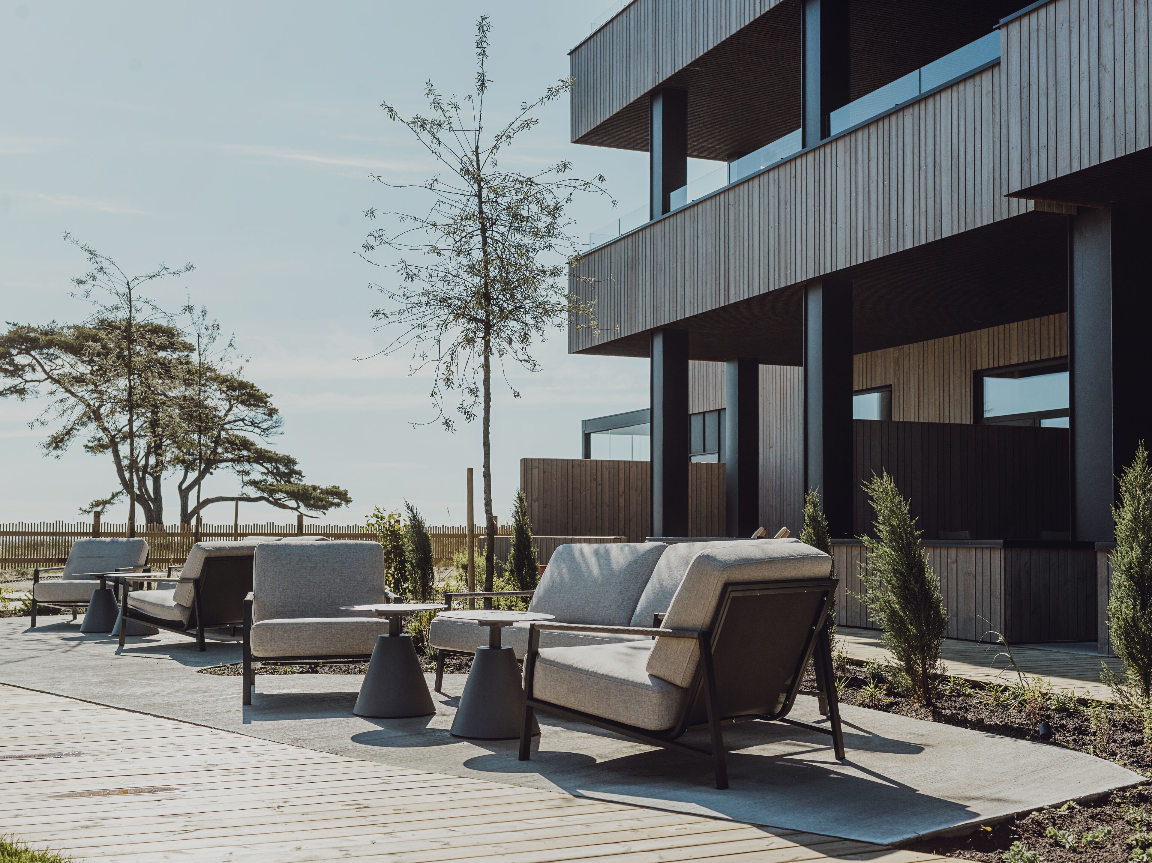 Uma área externa com mobiliário moderno, um deck de madeira e um edifício contemporâneo com grandes janelas.