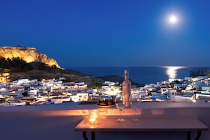 Uma mesa com garrafa e copos, com vista para uma cidade costeira à noite.