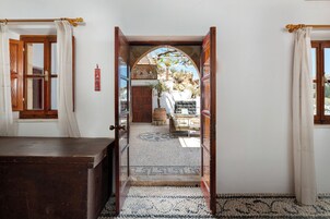 Uma porta aberta que dá para um pátio com piso estampado, um banco de madeira e um vaso com planta.