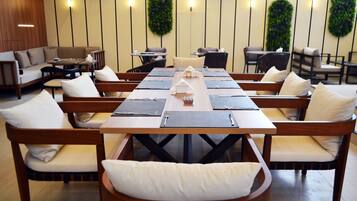 Uma sala de jantar com uma longa mesa de madeira posta para seis pessoas, rodeada por cadeiras de madeira com almofadas brancas.