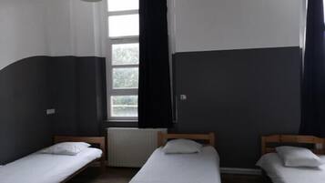 Quarto com três camas individuais, um radiador e uma janela com cortinas.