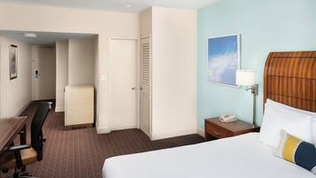 Quarto de hotel com cama, escrivaninha, cadeira e uma pequena cozinha.