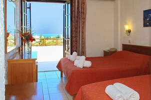 Quarto de hotel com duas camas, uma escrivaninha de madeira, um vaso com flores e vista para o oceano.