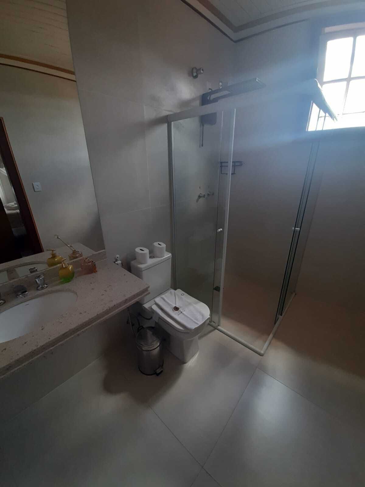 Casa de banho com cabine de duche em vidro, sanita e lavatório com dispensadores de sabonete.