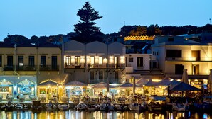 Uma área à beira-mar com barcos atracados, uma fileira de cafés e edifícios com varandas.