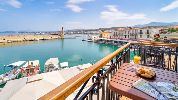 Um terraço à beira-mar com vista para o porto, barcos e edifícios.