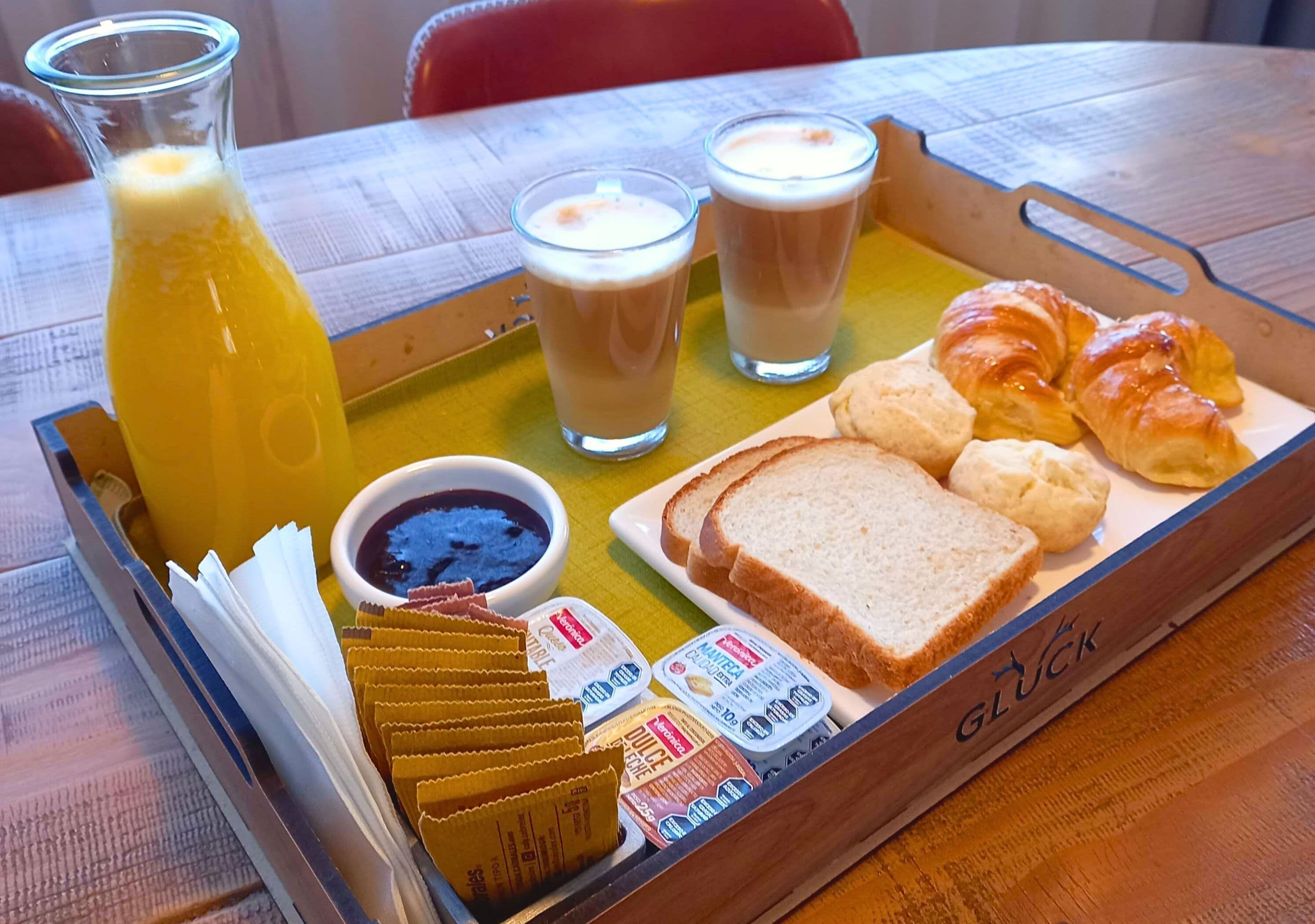 Uma bandeja com itens de café da manhã, incluindo croissants, pão, manteiga e suco.