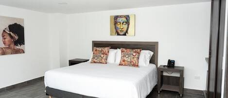 Quarto moderno com uma cama grande, duas mesas de cabeceira, uma obra de arte na parede e uma pequena mesa auxiliar com um telefone.