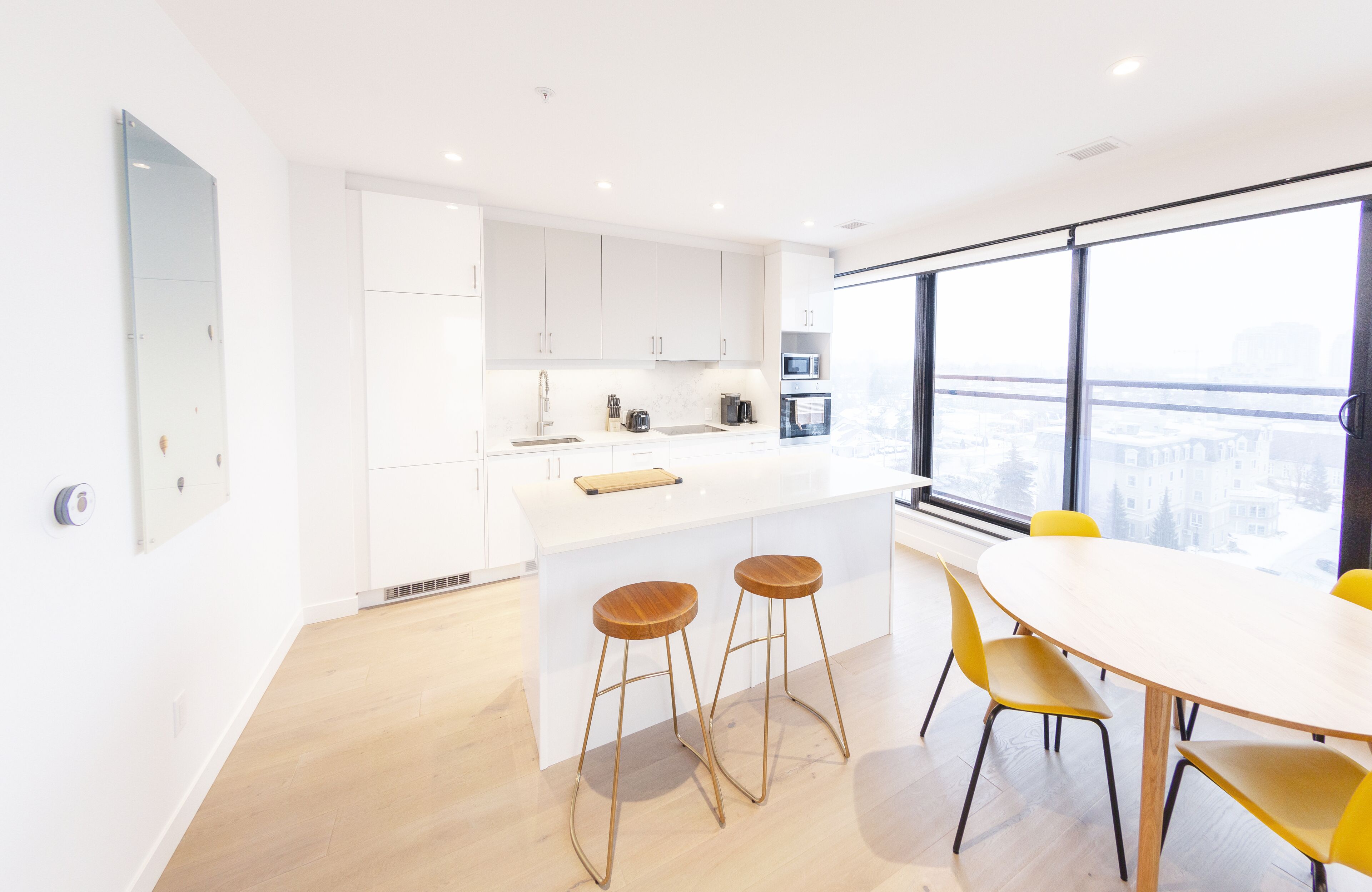 Uma cozinha moderna com armários brancos, uma ilha central com banquetas e uma mesa de jantar com cadeiras amarelas.