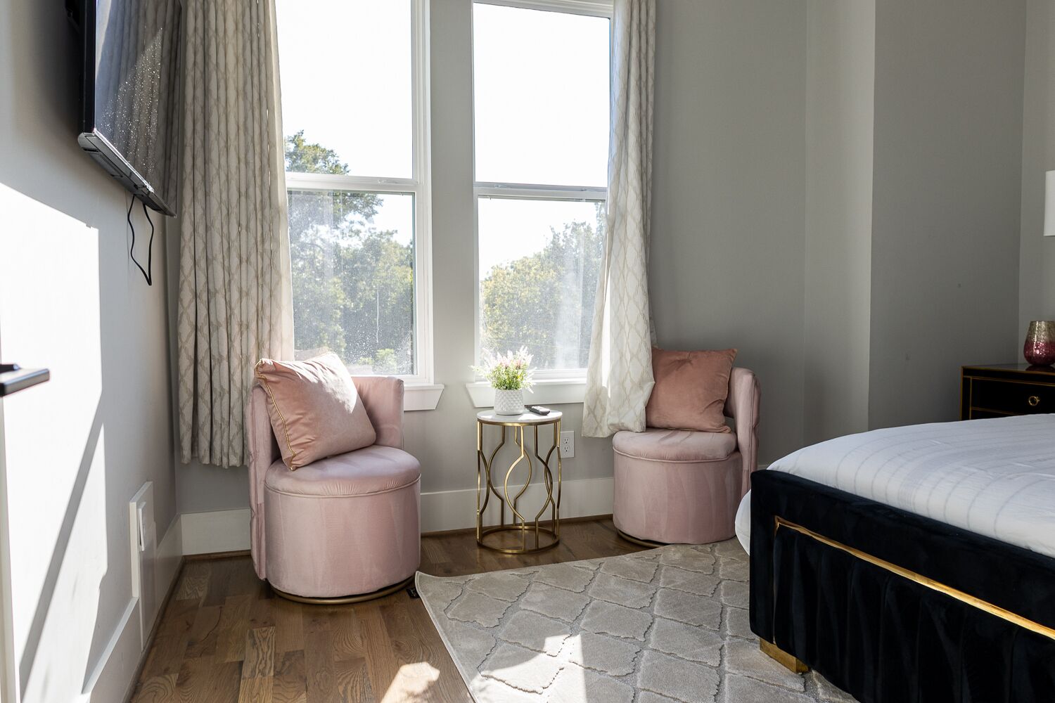 Quarto com cama, duas cadeiras cor-de-rosa, uma mesa pequena e janela com cortinas.