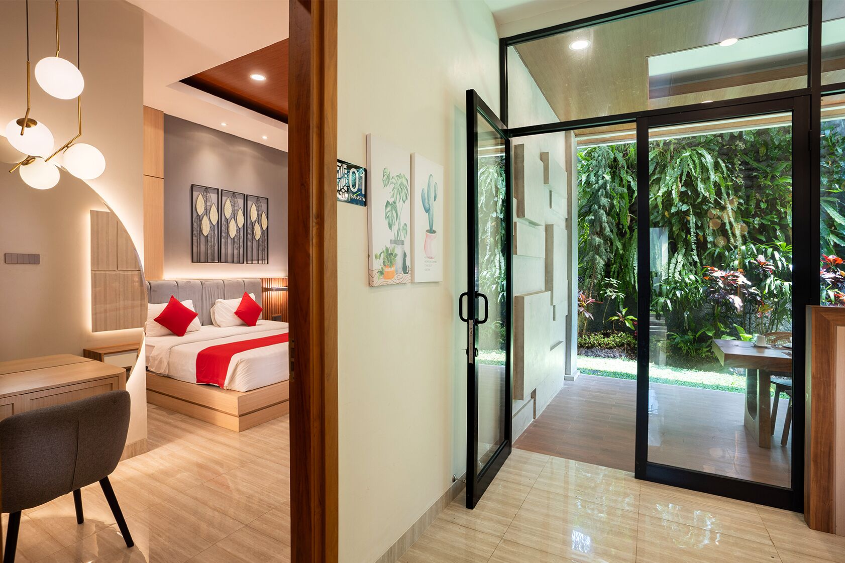Quarto de hotel moderno com cama, mesa de cabeceira e escrivaninha. Há uma porta de vidro que dá para um jardim com plantas.