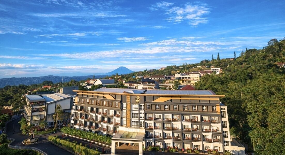 Hotel de vários andares com um pátio central, rodeado por vegetação exuberante e uma montanha ao fundo.