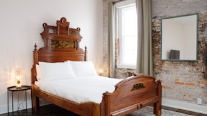 Uma cama de madeira num quarto com parede de tijolos e uma janela grande.