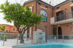 Um edifício de tijolos com uma fonte de pedra, uma piscina e uma árvore à frente.