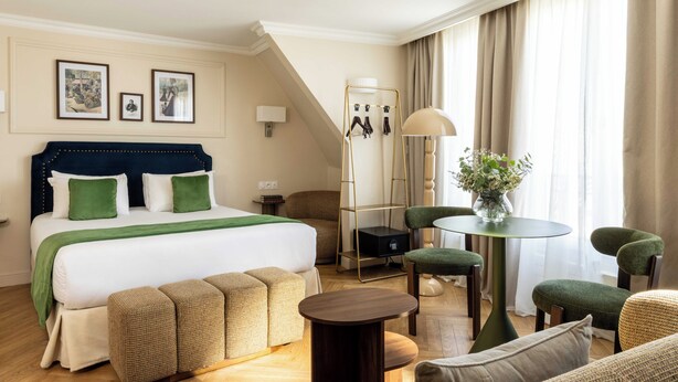 Quarto de hotel com cama, escrivaninha, cadeira e mesa.