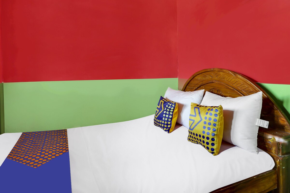 Cama com roupa de cama branca, cabeceira de madeira e duas almofadas estampadas.