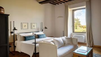 Quarto com uma cama, sofá branco, mesa de centro de vidro e janela com cortinas.