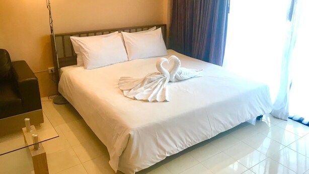 Quarto de hotel com uma cama bem arrumada, uma luminária e uma cadeira.