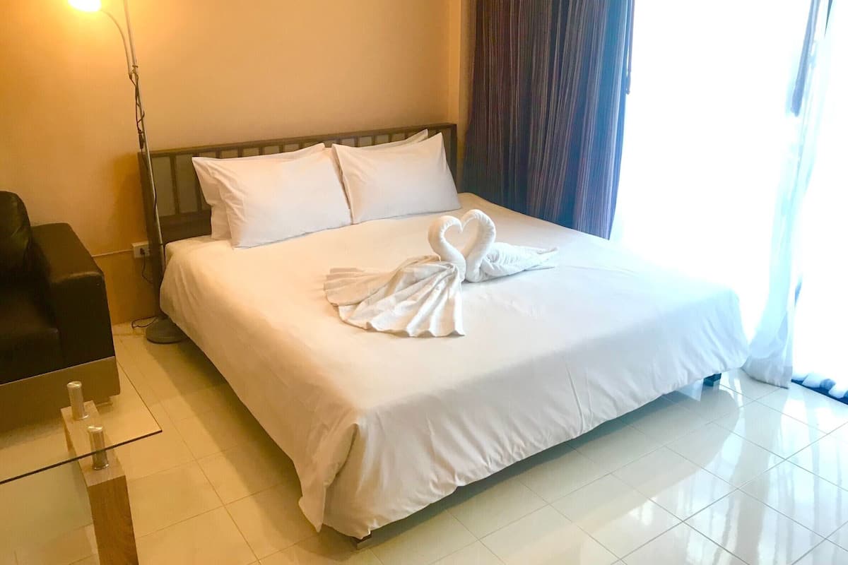 Quarto de hotel com uma cama bem arrumada, uma luminária e uma cadeira.