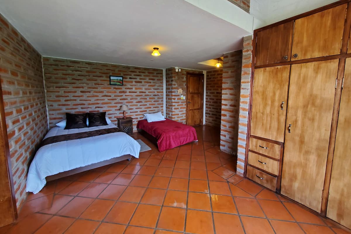 Quarto com duas camas, um guarda-roupa de madeira e uma parede de tijolos.