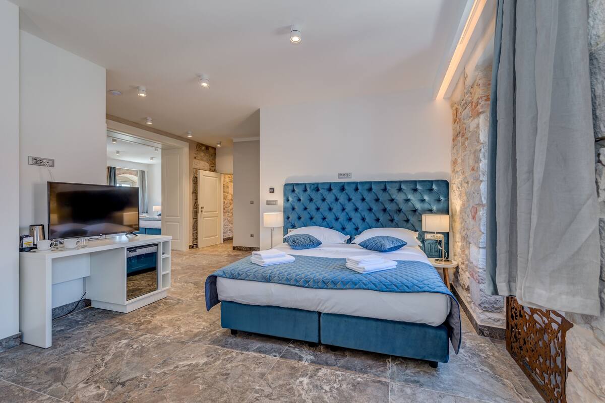 Quarto com cama, televisão, escrivaninha e parede de pedra.