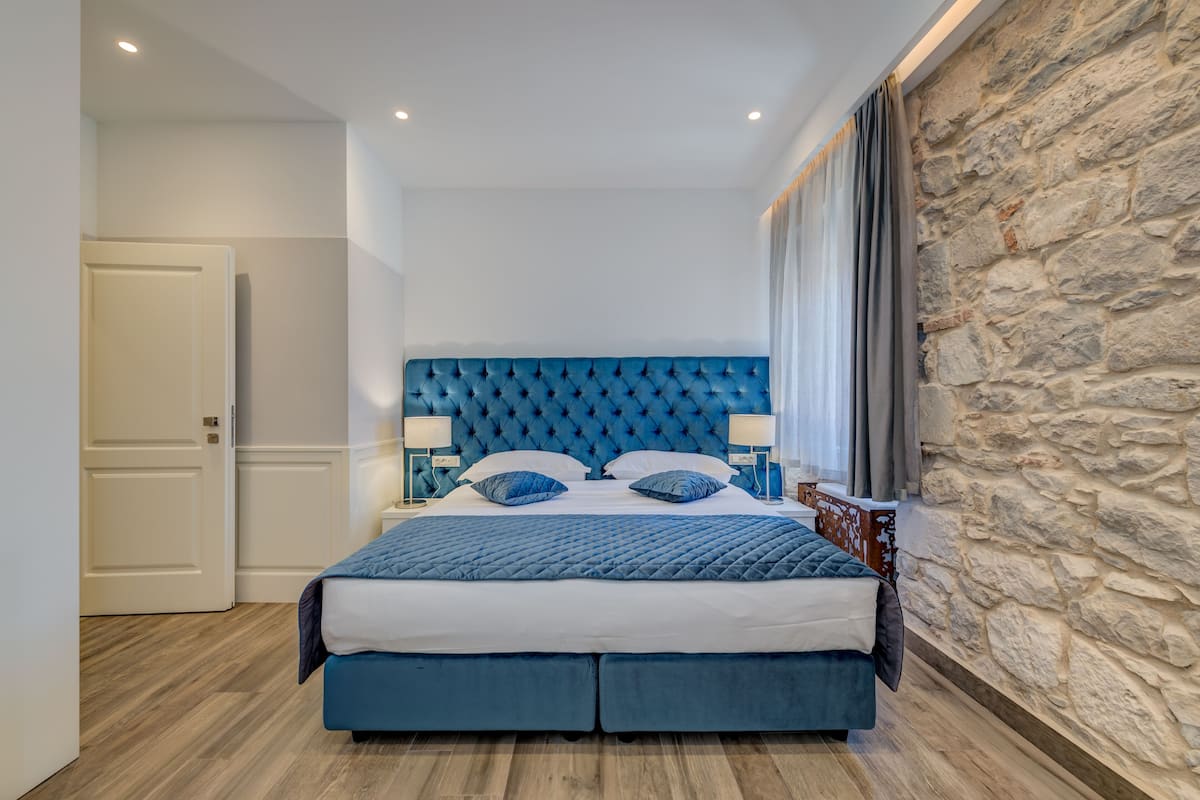 Quarto com uma cama grande, parede de pedra e uma porta.