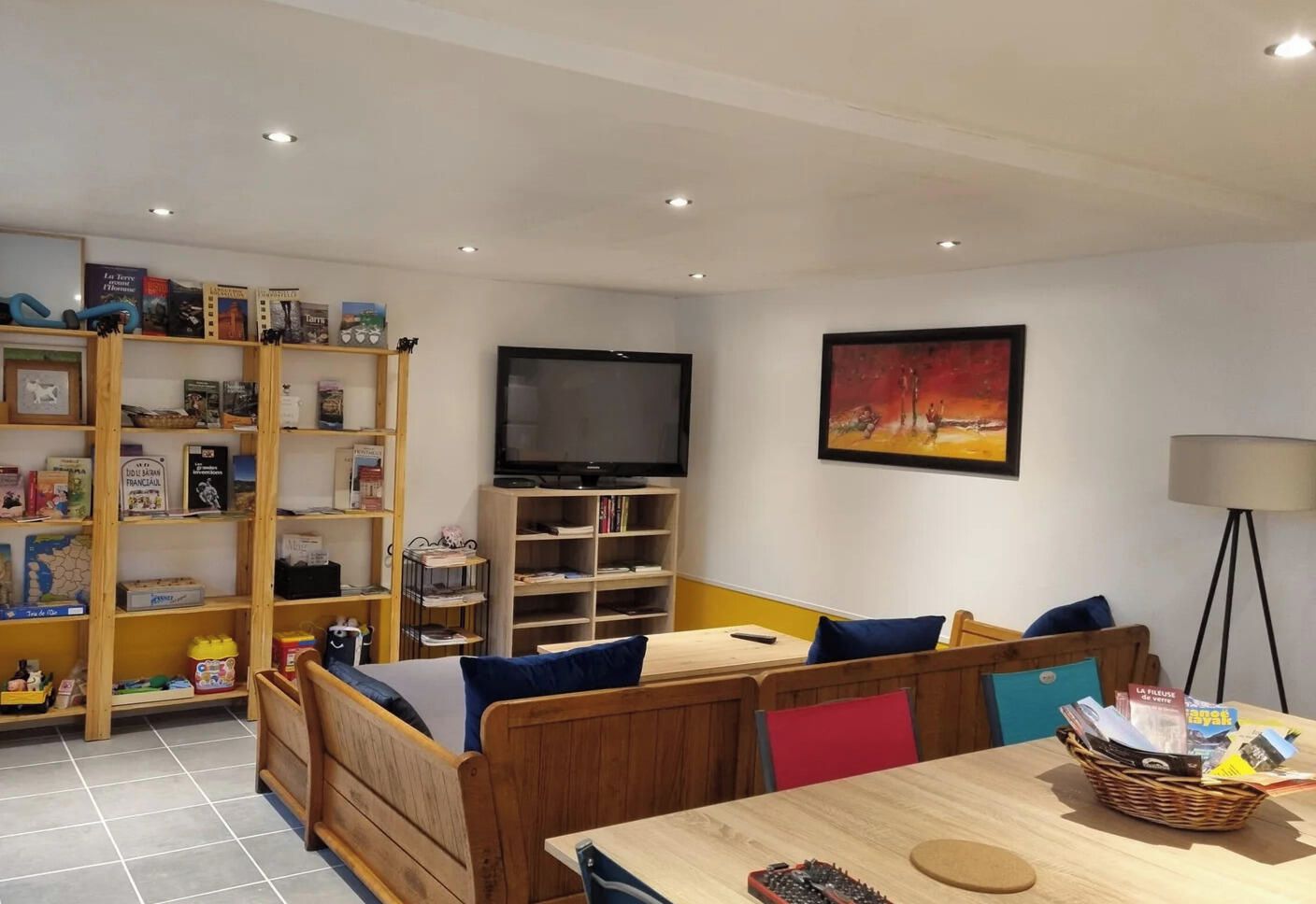 Uma sala de estar com televisão, estante de livros e um quadro na parede.