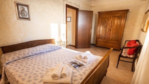 Quarto de hotel com cama, guarda-roupa de madeira, uma cadeira e um quadro na parede.