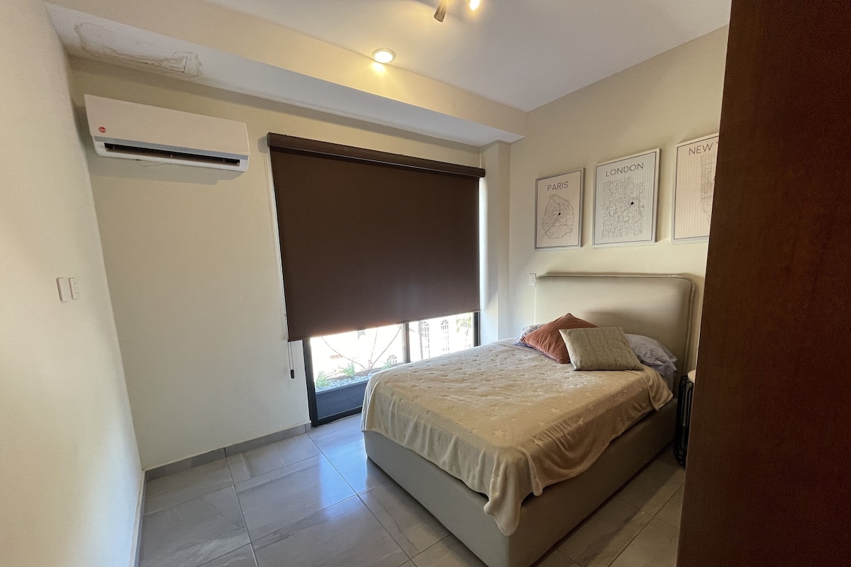 Quarto com cama, janela com persianas, luminária no teto e ar-condicionado fixado na parede.