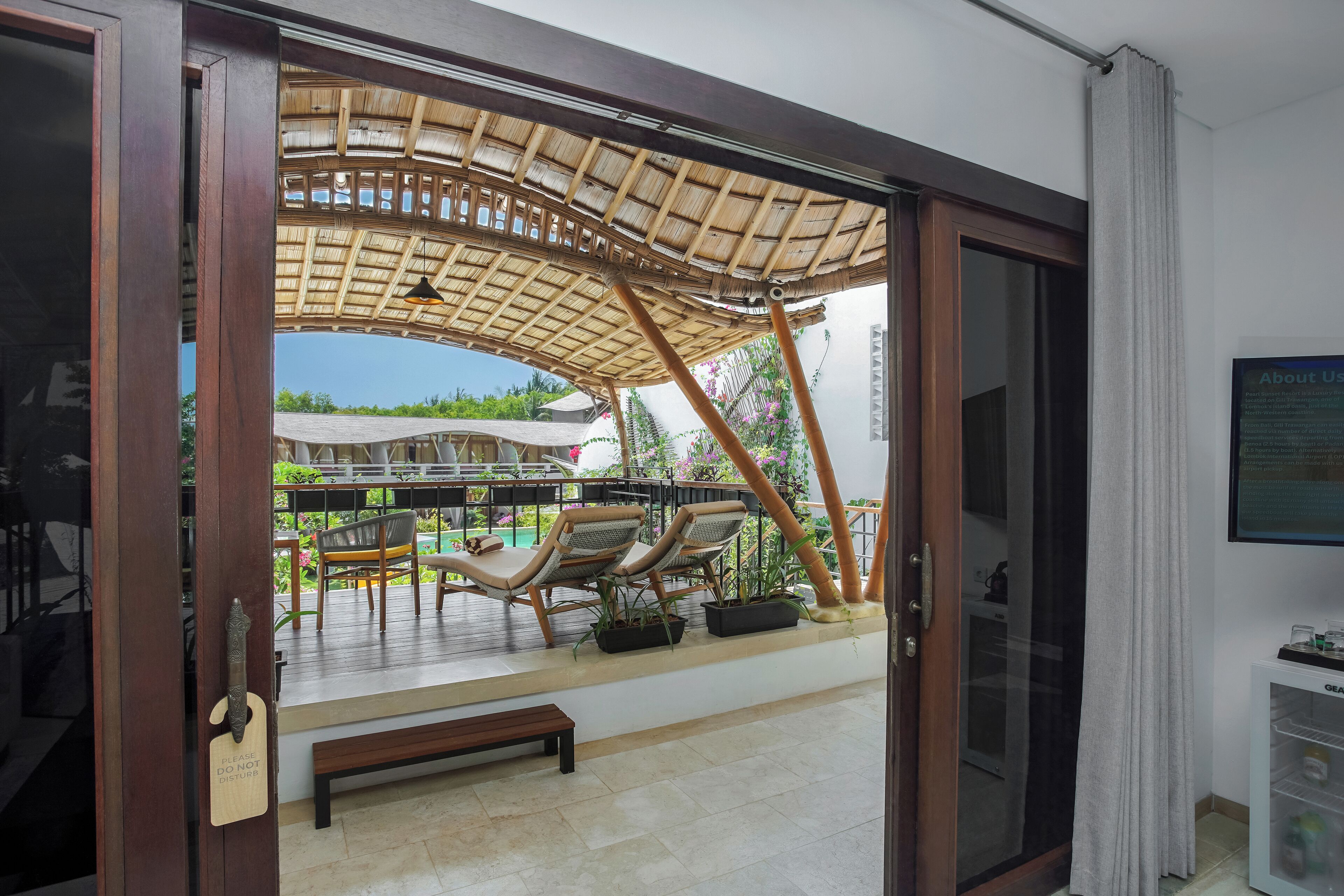 Quarto com porta de vidro que dá para área externa com teto de bambu, piscina e espreguiçadeiras.