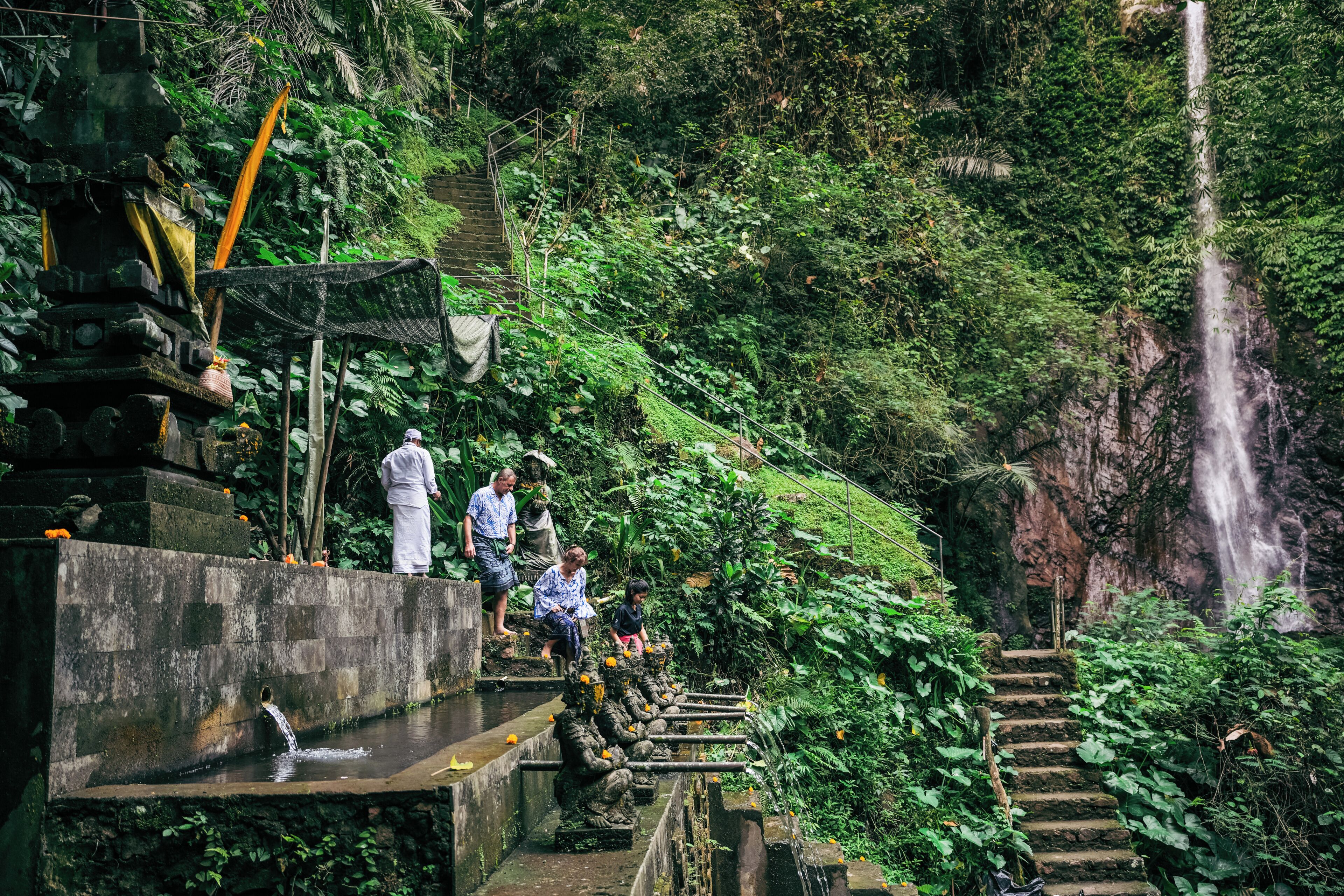 Uma escadaria de pedra leva a uma cascata rodeada por vegetação exuberante.