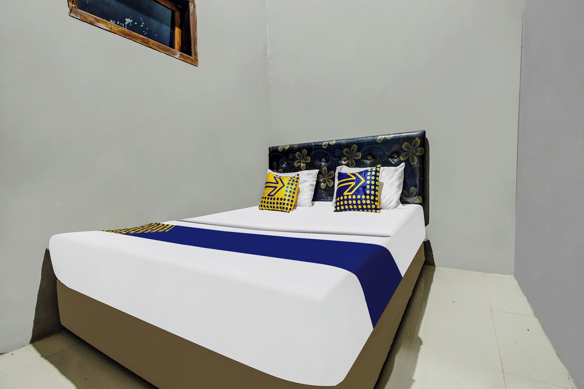 Uma cama com edredom branco e azul, cabeceira escura com estampas florais e duas almofadas com desenhos em amarelo e azul.