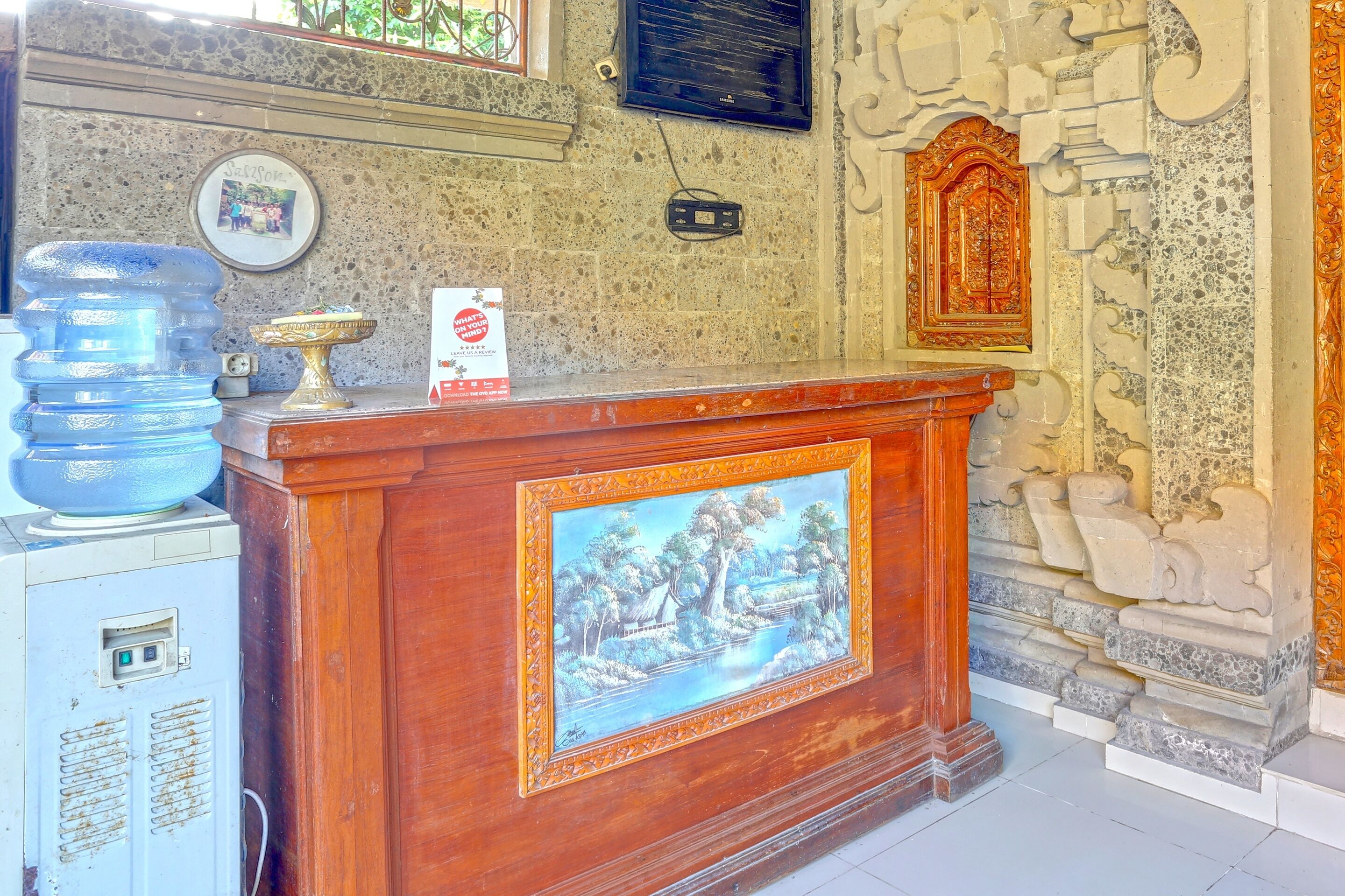 Balcão de recepção com um quadro emoldurado, um bebedouro, um rádio e uma placa.
