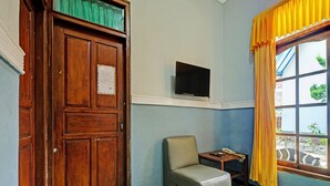 Quarto com guarda-roupa de madeira, televisão na parede, mesa pequena com telefone e janela com cortinas amarelas.