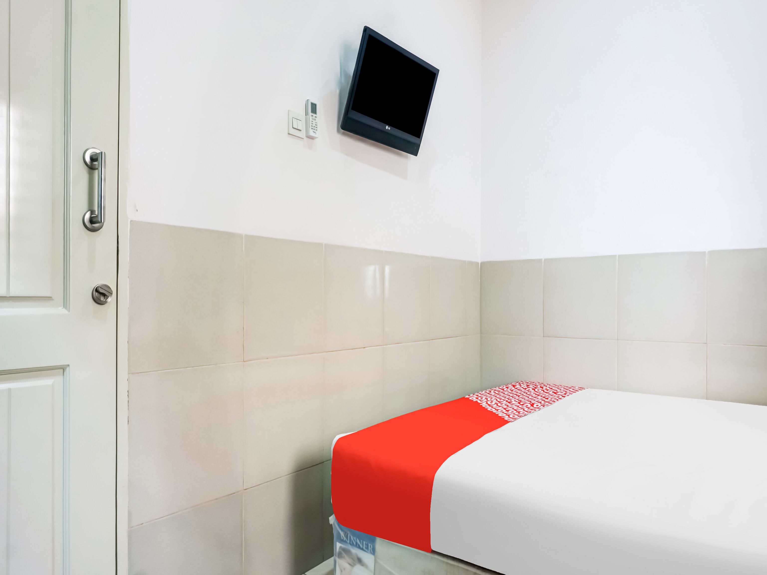 Quarto de hotel com cama, televisão fixada na parede e porta com puxador.