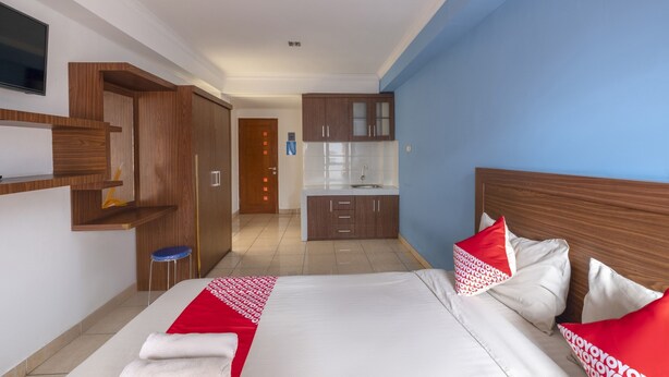 Quarto de hotel com cama, pequena escrivaninha, cozinha compacta e banheiro.