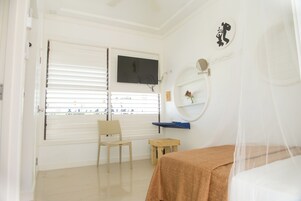 Quarto com cama, cadeira, televisão, espelho e janela com persianas.